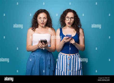 Two Twins With Curly Hair Posing Shocked With Mobiles On Blue Studio Wall Stock Photo Alamy