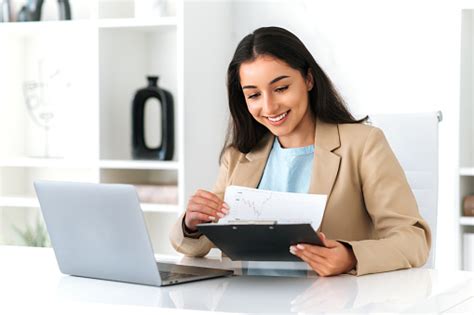 긍정적이고 우아한 성공한 인도 또는 아라비아 비즈니스 우먼 사무실의 직장에 앉아있는 재무 관리자 노트북으로 작업 재무 보고서를 공부하고 결과에 기뻐하고 미소 짓는 행복에