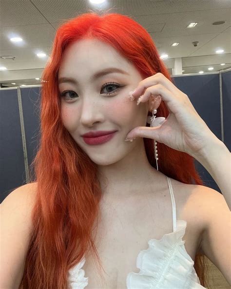 A Woman With Long Red Hair Wearing A White Dress And Holding Her Hand Up To Her Ear