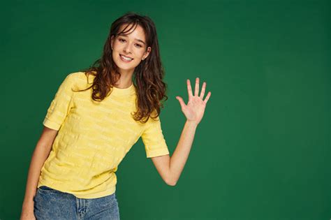 친절한 소녀 블로거가 인사말 제스처로 손을 흔들며 녹색 스튜디오 배경에서 구독자를 환영하는 미소를 지었습니다 인사하기에 대한 스톡 사진 및 기타 이미지 Istock