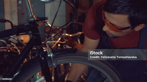 테마 중소 기업 자전거 수리 보호 안경 장갑과 Fartuhe에 젊은 갈색 머리 백인 남자는 수리 및 차고 작업장에서 림 브레이크와 바퀴 회전 자전거를 튜닝하기 위해 손
