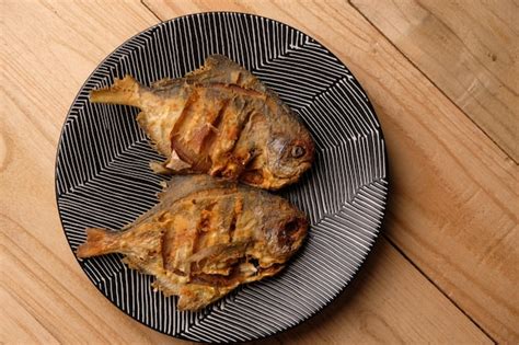 Premium Photo Fried Pomfret Fish On A Black Ceramic Plate On Wooden