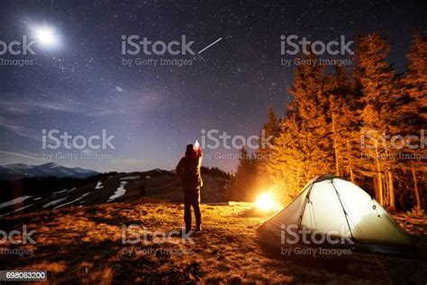 남성 관광 밤에 그의 캠프에 있는 나머지가 있다 캠프 파이어 및 아름 다운 밤 하늘 별과 달의 전체 아래 텐트 근처에 서 고 공간 위성을 지구 궤도 진입에서 남자 가리키기에