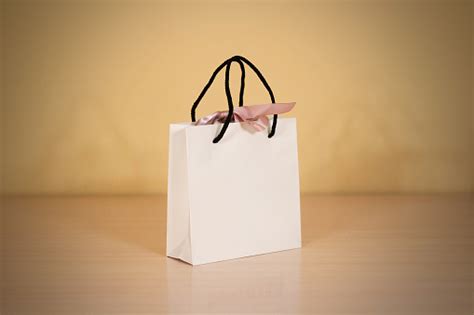 나무 테이블에 서있는 활 모의 빈 흰색 종이 선물 가방 빈 플라스틱 패키지 모형은 테이블 에 격리 로고 디자인 또는 아이덴티티 프리젠 테이션을위한 소비자 팩 준비 가방에