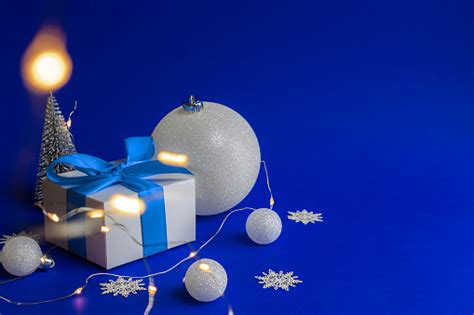 크리스마스 장식품 파란색 리본 겨울 나무 눈송이 실버 볼이 있는 흰색 선물 상자가 파란색 배경에 있는 크리스타 장식으로 인사말 카드를 제공합니다 겨울 축제 구성 복사 공간