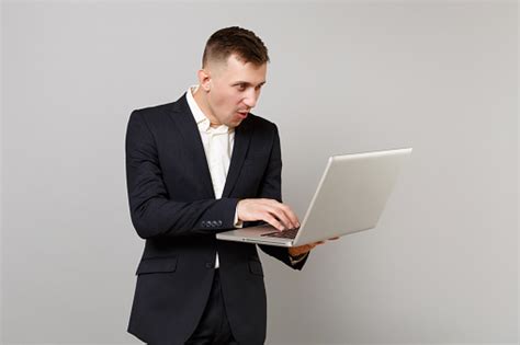 클래식 블랙 정장에서 젊은 비즈니스 남자를 깜짝 놀라게 흰색 셔츠 스튜디오에서 회색 벽 배경에 고립 된 노트북 Pc 컴퓨터에서