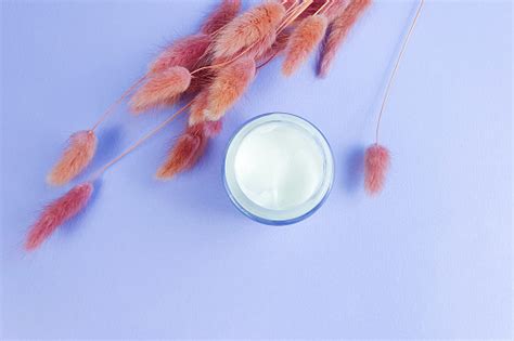 화이트 모이스처라이저 페이셜 또는 아이 크림은 오픈 글래스 항아리에 질감이 있는 보라색 배경의 핑크 라구루 복사 공간이 있는