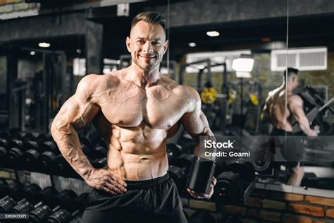 근육질의 보디 빌딩 운동 선수는 완벽한 몸을 가지고 단백질 또는 유청 항아리 모형을 들고 체육관 몸통을 가진 운동 선수 피트니스 클럽에서 몸통을 가진 남자 스포츠 영양 및