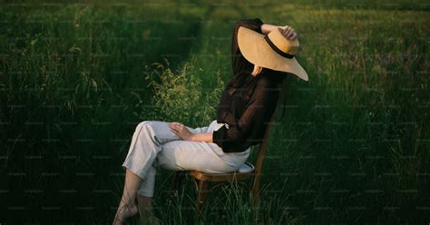 느린 생활 밀짚모자를 쓴 세련되고 우아한 소녀는 저녁 햇살을 받으며 여름 푸른 초원의 소박한 의자에 앉아 있다 들판에서 휴식을 취하는 세련된 젊은 여성 고요한 순간