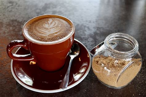 검은 나무 테이블 배경에 우유 거품과 유리 설탕 용기에 갈색 설탕과 빨간 컵에 핫 카푸치노 신선한 커피를 탑 뷰 음료 개념입니다