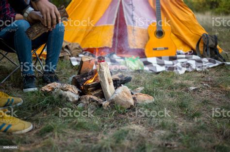 아름 다운 커플 앉아 캠프 파이어 주위에 캠핑 텐트와 배경에 남자 막대기로 화재 제스처 건강한 생활방식에 대한 스톡 사진 및 기타 이미지 Istock