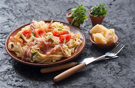 블랙 슬레이트 배경에 베이컨 계란 파마산 치즈와 바 질이 있는 클래식 파스타 카르보나라 테이블 옆에는 파마산 치즈 바 질 포크 조각이 놓여 있습니다 고기에 대한 스톡 사진