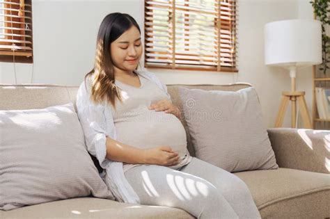 Young Pregnant Touching Her Belly while Woman Sitting on Couch in ...