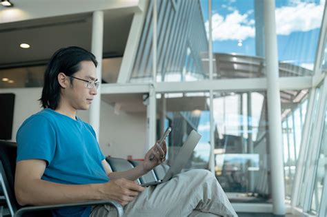 공항에서 출발하는 비행기를 기다리면서 스마트폰과 노트북으로 작업하는 아시아 남성 30 34세에 대한 스톡 사진 및 기타 이미지 30 34세 Brand Name