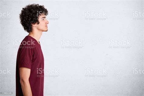 프로필 샷 어두운 곱슬 머리와 잘생긴 젊은 남자 캐주얼 마 룬 T 셔츠를 입고 복사 공간을 보면 광고 또는 홍보 텍스트에 대 한 여유 공간 흰 벽에 대 한 의미 남자에 대한