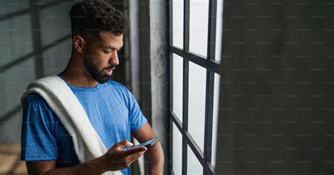 젊은 아프리카계 미국인 스포츠맨이 체육관에서 실내에 서서 스마트폰과 스마트워치를 사용하고 있다 사진 Unsplash의