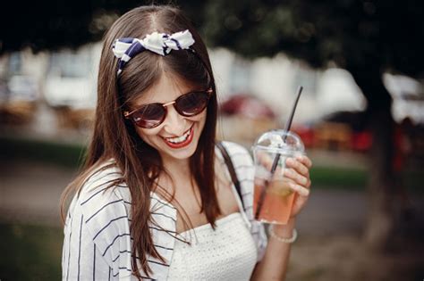 아름 다운 세련 된 젊은 여자 차가운 음료를 들고 도시 거리에 웃 고 행복 한 Hipster 여자 선글라스 레트로 드레스 단일 사용 플라스틱 컵과 빨 대를 들고 개념에 대한