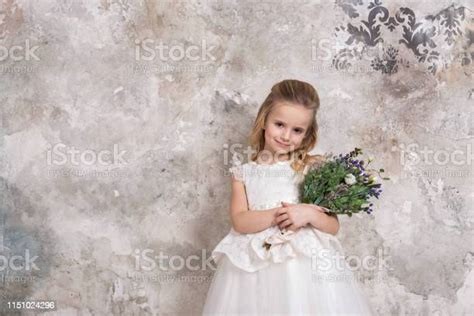 그런 지 벽의 배경에 대해 그녀의 손에 꽃다발 흰 드레스에 작은 매력적인 소녀의 Nportrait 텍스트 공간을 갖춘 스튜디오