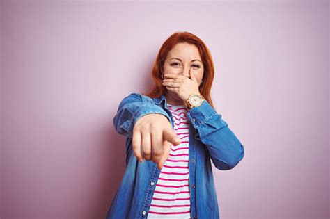 아름다운 빨간 머리 여자 데님 셔츠와 스트라이프 티셔츠 를 입고 고립 된 분홍색 배경에 웃음 입에 손으로 카메라에 손가락을 가리키는 수치표정 T 셔츠에 대한 스톡 사진 및