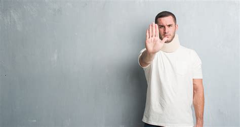 젊은 백인 남자가 심각 하 고 자신감 표현 방어 제스처 정지 표시를 하 고 오픈 손으로 목 칼라를 입고 회색 그런 지 벽 위로 부상 건강관리와 의술에 대한 스톡 사진 및