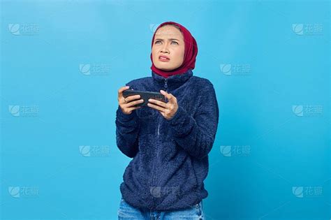 一名震惊的年轻亚洲女子正在玩智能手机上的视频游戏，抬头看蓝色的背景素材 花瓣网