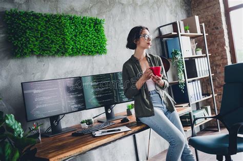 Focused Female Programmer In Casual Workspace Holding Coffee And Coding