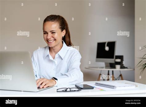 Brunette Woman Smiling While Working On Laptop In The Office Telecommuting Networking Virtual