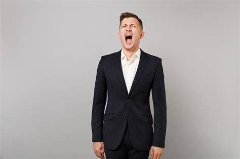 고전적인 검은 양복에 좌절 젊은 사업가 셔츠는 눈을 감고 스튜디오에서 회색 벽 배경에 고립 비명을 유지 업적 경력 자산 사업