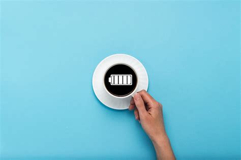 파란색 배경에 검은 커피와 흰색 컵을 들고 여성의 손 충전된 배터리의 부호입니다 하루에 대한 개념 요금 플랫 레이 상단 보기