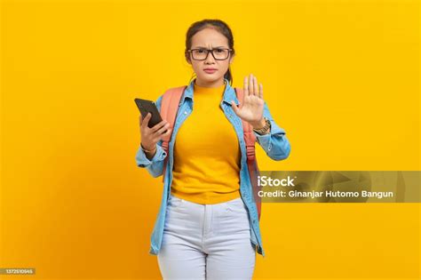 배낭을 들고 노란 배경에 고립 된 정지 제스처를 보여주는 배낭으로 캐주얼 한 옷을 입은 젊은 아시아 여성 학생의 초상화 모던 양식에 대한 스톡 사진 및 기타 이미지 Istock