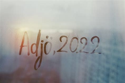 스웨덴어로 된 글자 Adjo는 영어로 작별 인사를 하고 2022년 숫자는 일몰 창에 비에 의해 뿌려진 물에 손가락으로