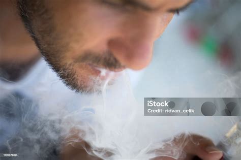 한 남자가 회색 배경에서 전자 담배를 피우고 연기의 흐름을 불어 넣습니다 남자에 대한 스톡 사진 및 기타 이미지 남자 남자들만 전자담배 Istock