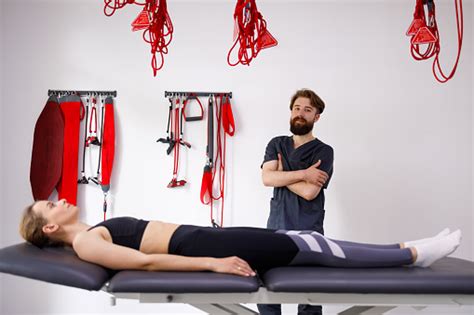 교차 된 팔을 가진 의사 물리 치료사 재활 학자는 사무실의 소파에 누워있는 여성 환자 옆에 서 있습니다 20 24세에 대한 스톡 사진 및 기타 이미지 Istock