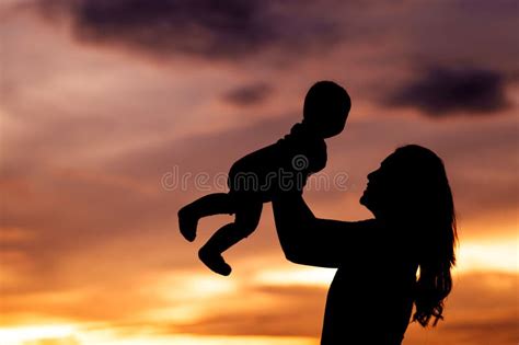 Silueta De La Madre Sosteniendo Y Levantando Con El Bebé Al Atardecer