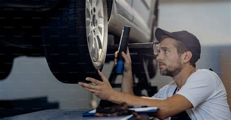 자동차 수리점에서 일하는 동안 손전등으로 자동차 타이어를 검사하는 중년 성인 정비사 사진 Unsplash의 세르비아 이미지