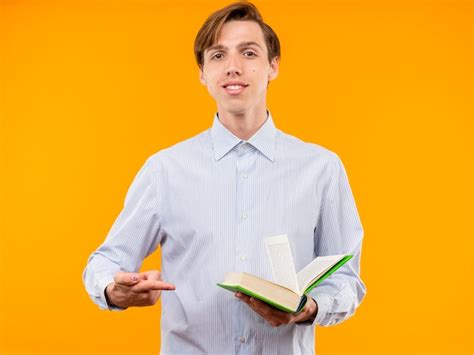 Молодой человек в белой рубашке держит открытую книгу улыбаясь