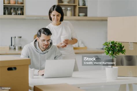 신혼 부부의 사진은 새로운 구입 한 집을 가구에 대해 생각 현대 노트북 컴퓨터에서 인터넷에서 몇 가지 아이디어를 검색 테이크 아웃 커피를 마시고 골판지 상자와 현대 부엌에서