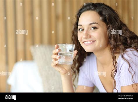Happy Woman Holding Water Glass Looks At You Sitting On A Bed Stock