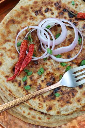 고추 붉은 양파 반지 다진 부추를 얹은 알루 파라타 더미가 있는 금속 트레이의 풀 프레임 이미지 으깬 가람 마살라 감자와 금속 포크로 채워진 짭짤한 플랫브레드 높은 전망