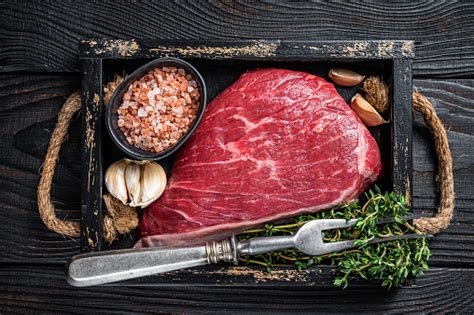 허브가 있는 나무 트레이에 고기 스테이크나 피칸하를 잘라낸 생 탑 등심 캡 쇠고기 검은 색 나무 배경 위쪽 보기 피카냐에 대한