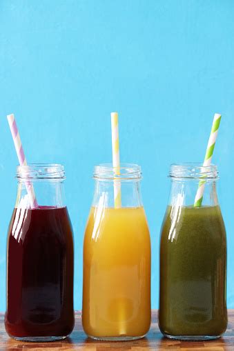 세 개의 유리 보라색 노란색 및 녹색 과일의 스크류 캡 병과 식용 빨대를 벗긴 야채 주스 스무디 파란색 배경 전경에 초점을 맞춘 행의 클로즈업 이미지 음식에 대한 스톡 사진