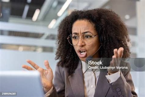 안경과 양복을 입은 젊은 화난 아프리카계 미국인 여성이 헤드셋을 착용한 노트북 화면을 향해 감정적으로 소리치는 클로즈업 사진 걱정하는에 대한 스톡 사진 및 기타 이미지