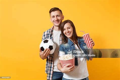 젊은 커플 여자 남자 축구 팬 들 들고 축구공 팝콘의 물통 플라스틱 유리 콜라의 재미 지원 팀 노란 배경에 고립 된 기운 스포츠