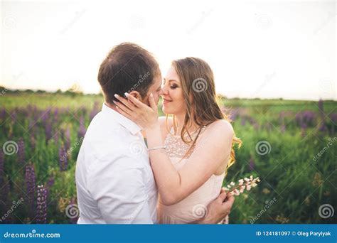 Bride Holds Groom`s Neck While He Kisses Her In The Rays Of Sunset