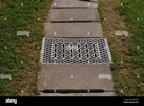 Iron Gutter With Grate Cover Of Drainage System On Pedestrian Walkway With Green Lawn On Summer