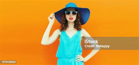 여름 밀짚 모자를 쓰고 포즈를 취하는 아름다운 젊은 여성 모델의 초상화 오렌지 색 배경에 파란색 드레스 여자에 대한 스톡 사진 및 기타 이미지 Istock