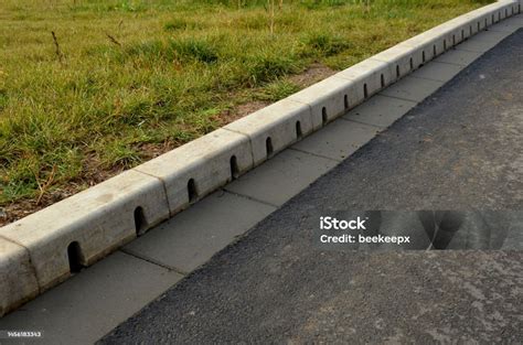 아스팔트 도로 가장자리에 숨겨진 배수 구멍이 뚫린 콘크리트 회색 연석에 숨겨진 배수 시스템 도로의 전체 길이를 따라 물이 구멍을 통해 하수구로 배수되고 잔디 묶기 연석에