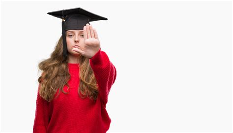 젊은 금발 여 자가 심각 하 고 자신감 표현 방어 제스처 정지 표시를 하 고 오픈 손으로 졸업 모자를 쓰고 경계 표지에 대한