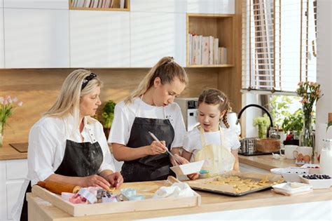 과정을 관리하는 노인 어머니 어린 큰 딸은 작은 것을 가르치고 쿠키 비스킷에 기름을 바르기 위해 그릇에 달걀을 털어내는 법을 가르칩니다 3 명에 대한 스톡 사진 및 기타