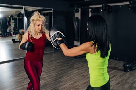 중년 여성은 체육관에서 개인 트레이너와 함께 훈련하고 권투 글러브를 착용하고 펀치를 날립니다 2명에 대한 스톡 사진 및 기타